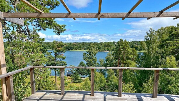 Um deck de madeira com guarda-corpo, com vista para um lago rodeado por árvores.