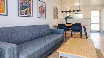 Uma sala de estar moderna com um sofá cinza, uma mesa de centro de madeira e uma área de jantar com mesa e cadeiras.