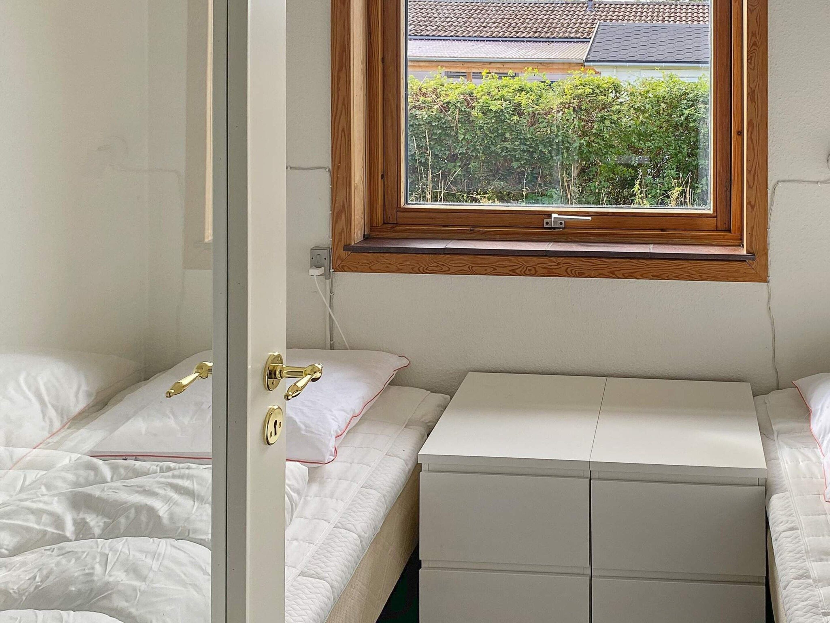 Quarto pequeno e aconchegante com duas camas, uma janela com vista para o verde e um peitoril de madeira.