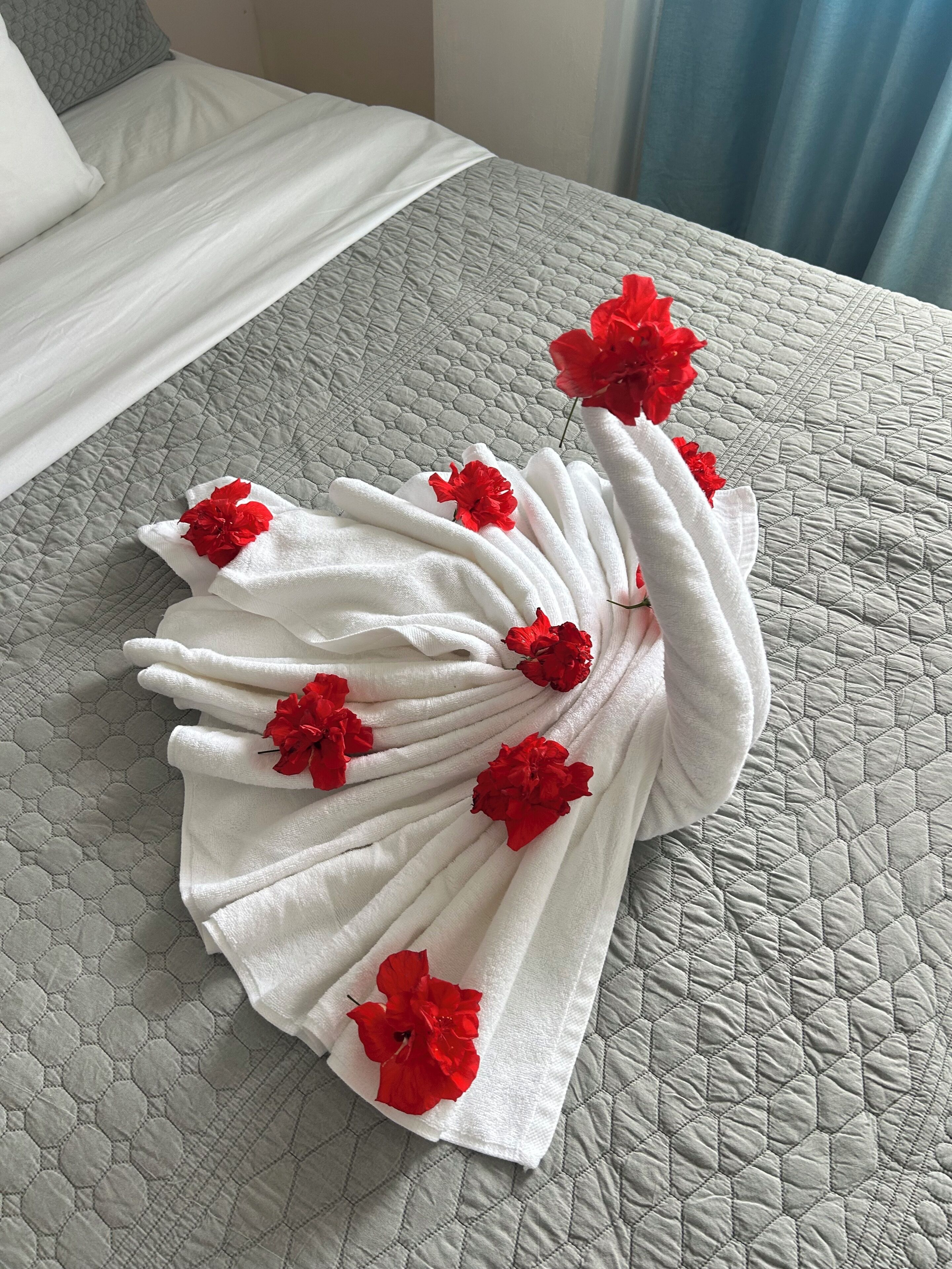 Uma toalha dobrada com flores vermelhas sobre uma cama com colcha cinza acolchoada.