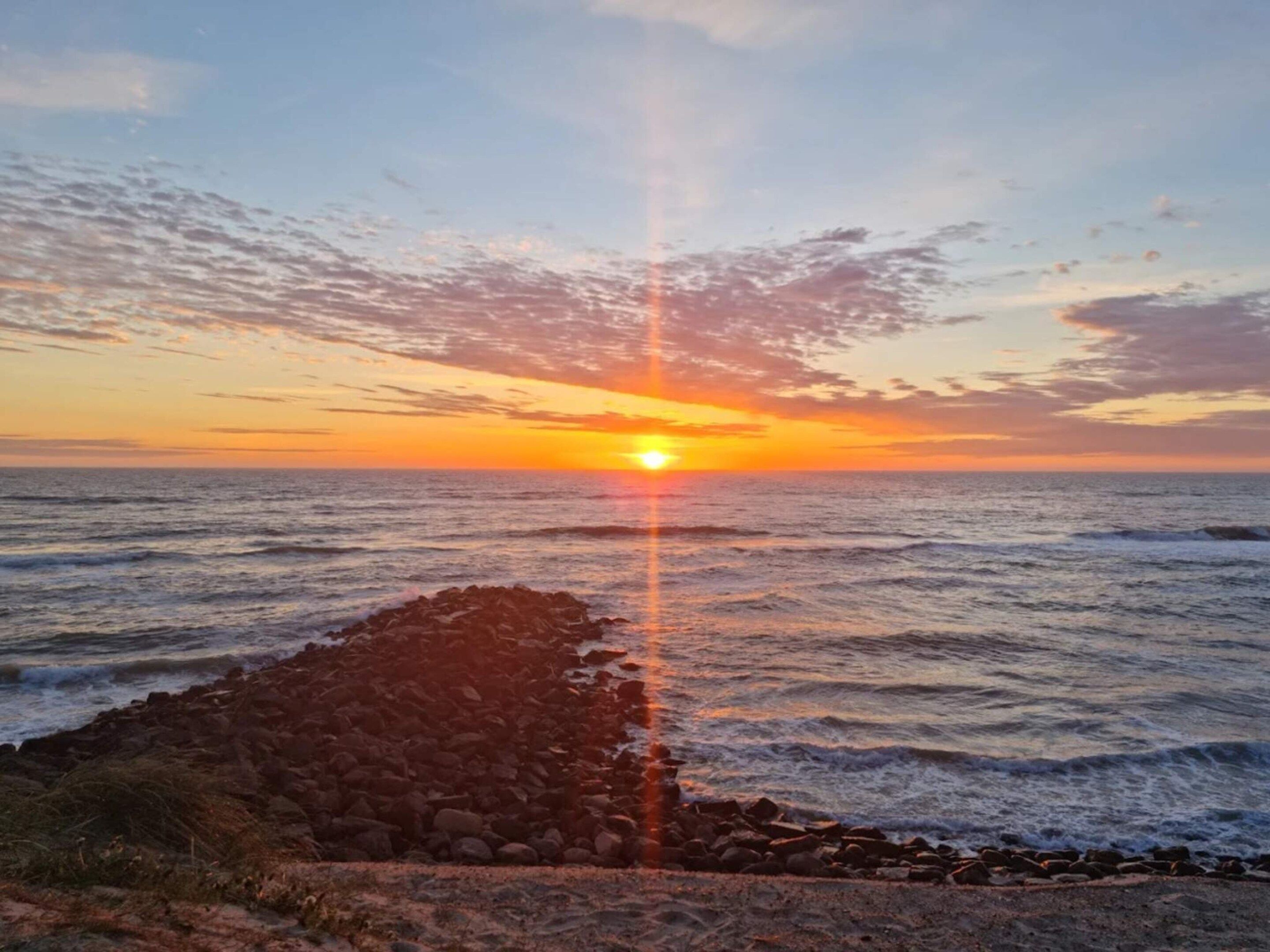 Um pôr do sol sobre uma costa rochosa com ondas.
