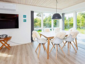 Uma sala de jantar moderna com mesa e cadeiras brancas, luminária pendente preta e vista para o verde lá fora.