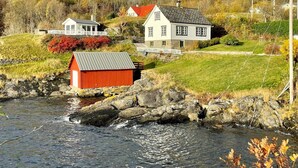Uma casa à beira-mar com um galpão vermelho, uma casa branca e um pequeno edifício branco com varanda.