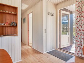 Um corredor com piso de madeira, uma prateleira de madeira com objetos, uma porta e uma janela com vista para árvores.