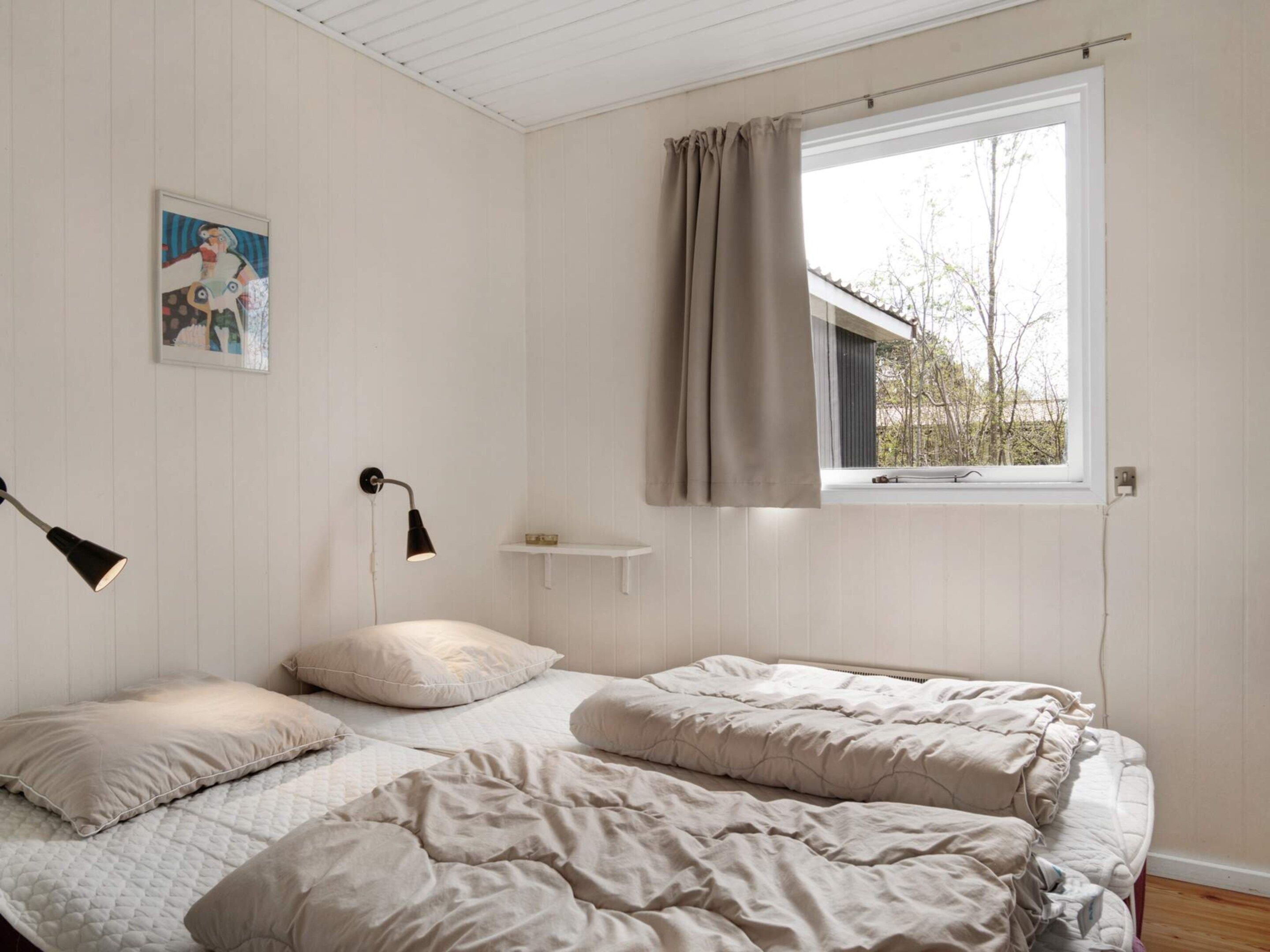 Quarto com cama, luminária de cabeceira, janela com cortinas e prateleira fixada na parede.