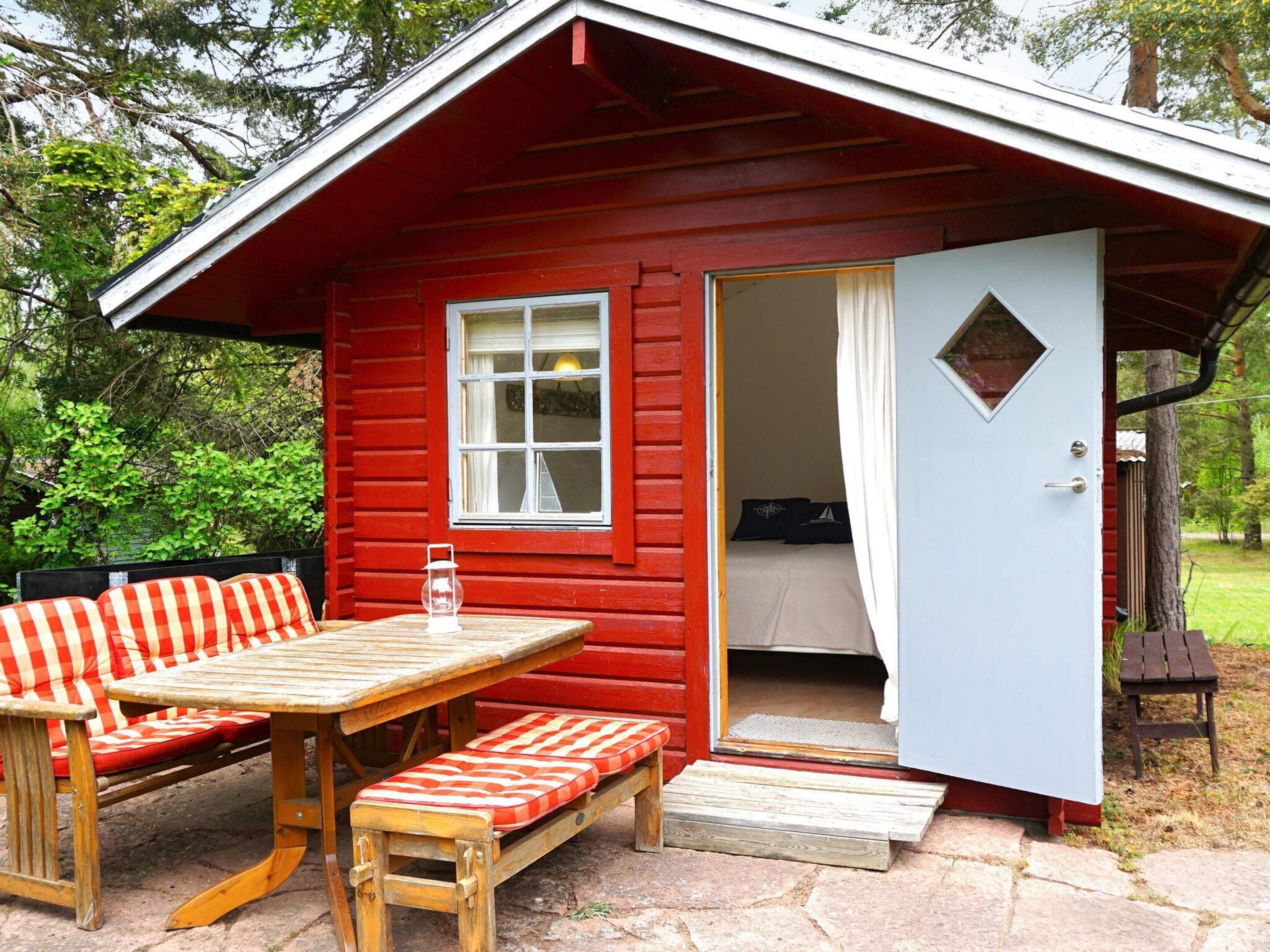 Uma cabana vermelha com uma mesa de madeira e almofadas listradas, uma janela e uma porta que dá para um quarto.