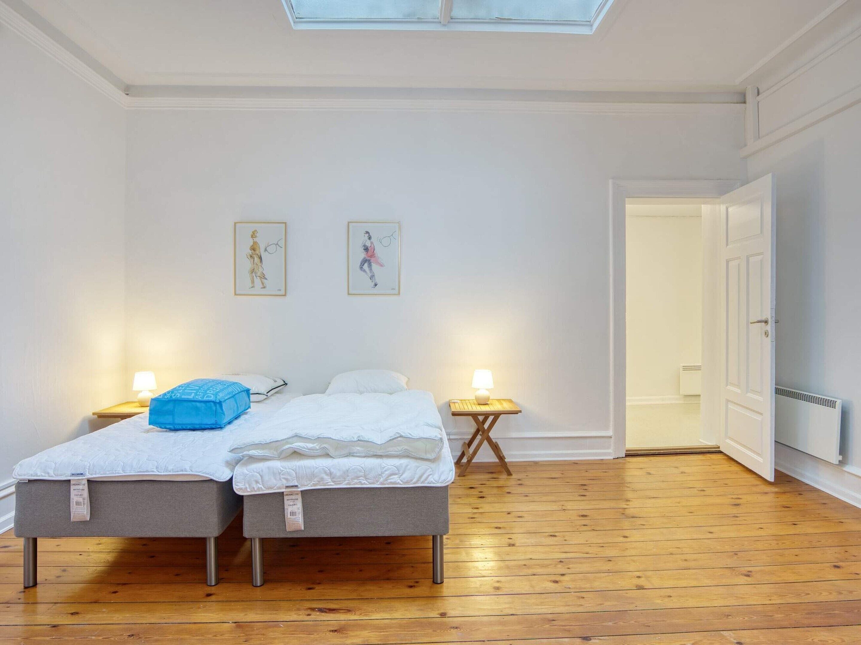 Quarto com duas camas, um claraboia e duas luminárias de parede.