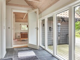 Quarto com teto de madeira, uma grande porta de vidro deslizante que dá para uma área externa, e um berço de bebê visível pela porta.