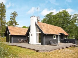 Uma cabana moderna com telhado inclinado, chaminé e um deck com mobiliário de exterior.