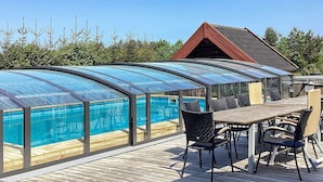 Piscina coberta com deck de madeira, móveis de exterior e um edifício ao fundo.