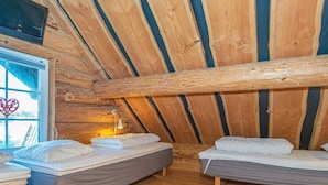 Uma cabana com duas camas, uma janela decorada com um coração e uma televisão fixada na parede.