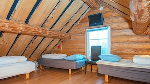 Quarto de sótão aconchegante com vigas de madeira, televisão e duas camas com almofadas.