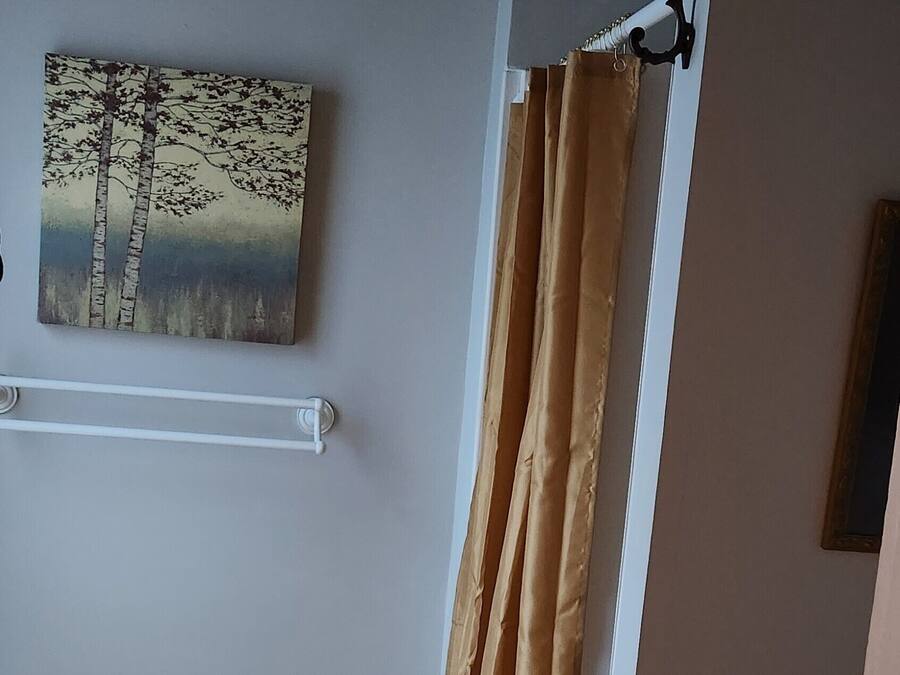 Um banheiro com piso bege, um radiador branco, um chuveiro com cortina bege e um quadro de árvores na parede.