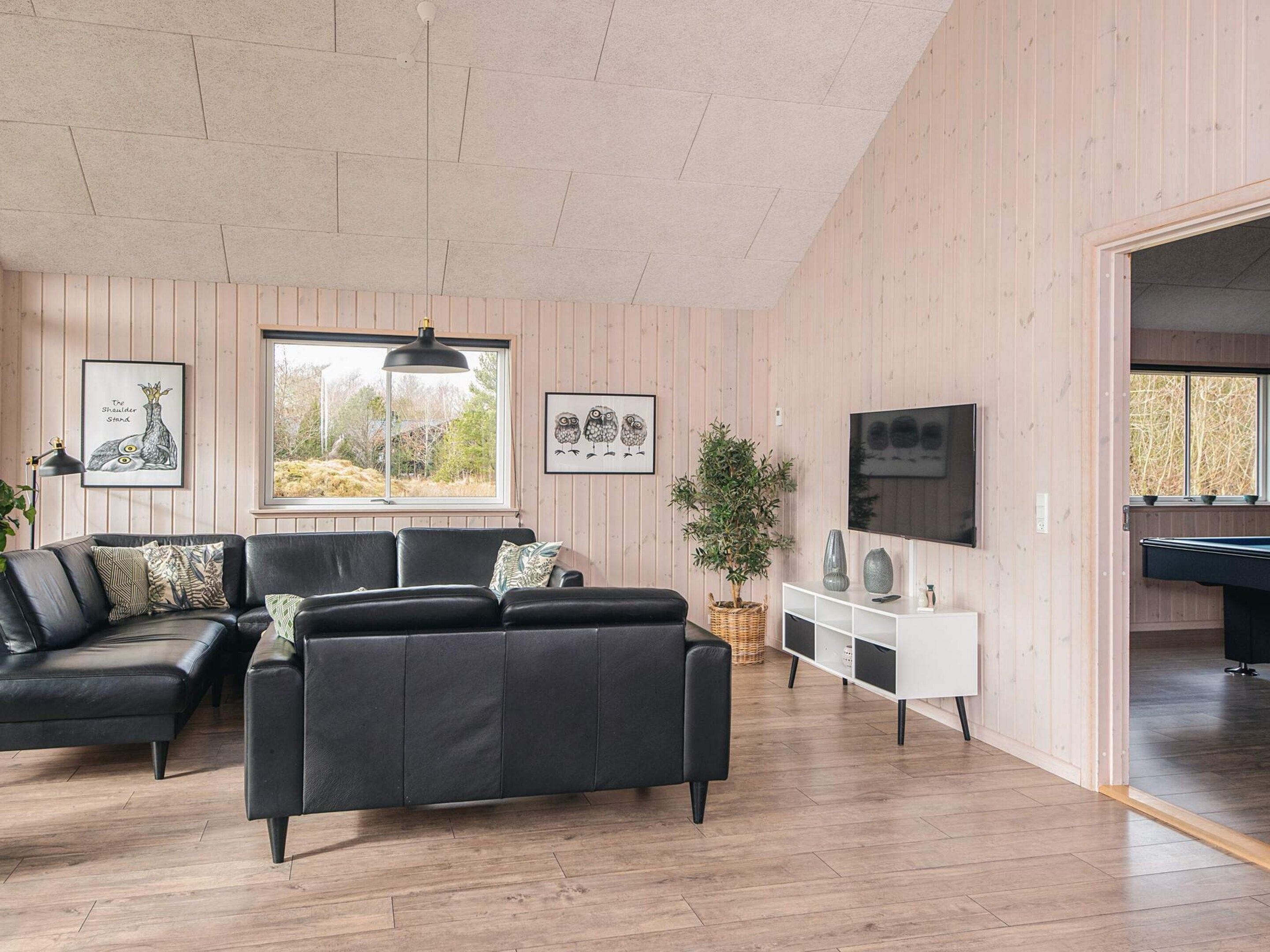 Uma sala de estar moderna com um sofá de couro preto, uma mesa de console branca e uma televisão na parede.