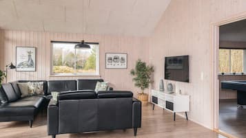 Uma sala de estar moderna com um sofá de couro preto, uma mesa de console branca e uma televisão na parede.