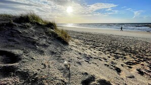 Uma praia com pegadas, uma pessoa caminhando e um céu claro.