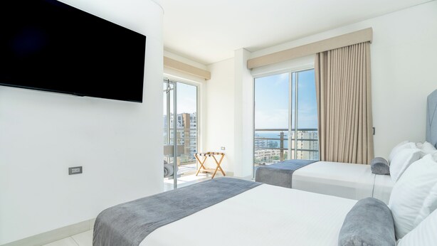 Quarto de hotel com duas camas, televisão de tela plana na parede e varanda vista para a cidade.