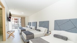 Quarto de hotel com três camas, televisão na parede e vista para a varanda.