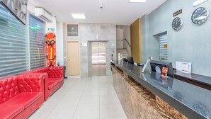 Uma área de recepção com um sofá vermelho, um balcão de atendimento, um relógio e uma placa indicando a localização.
