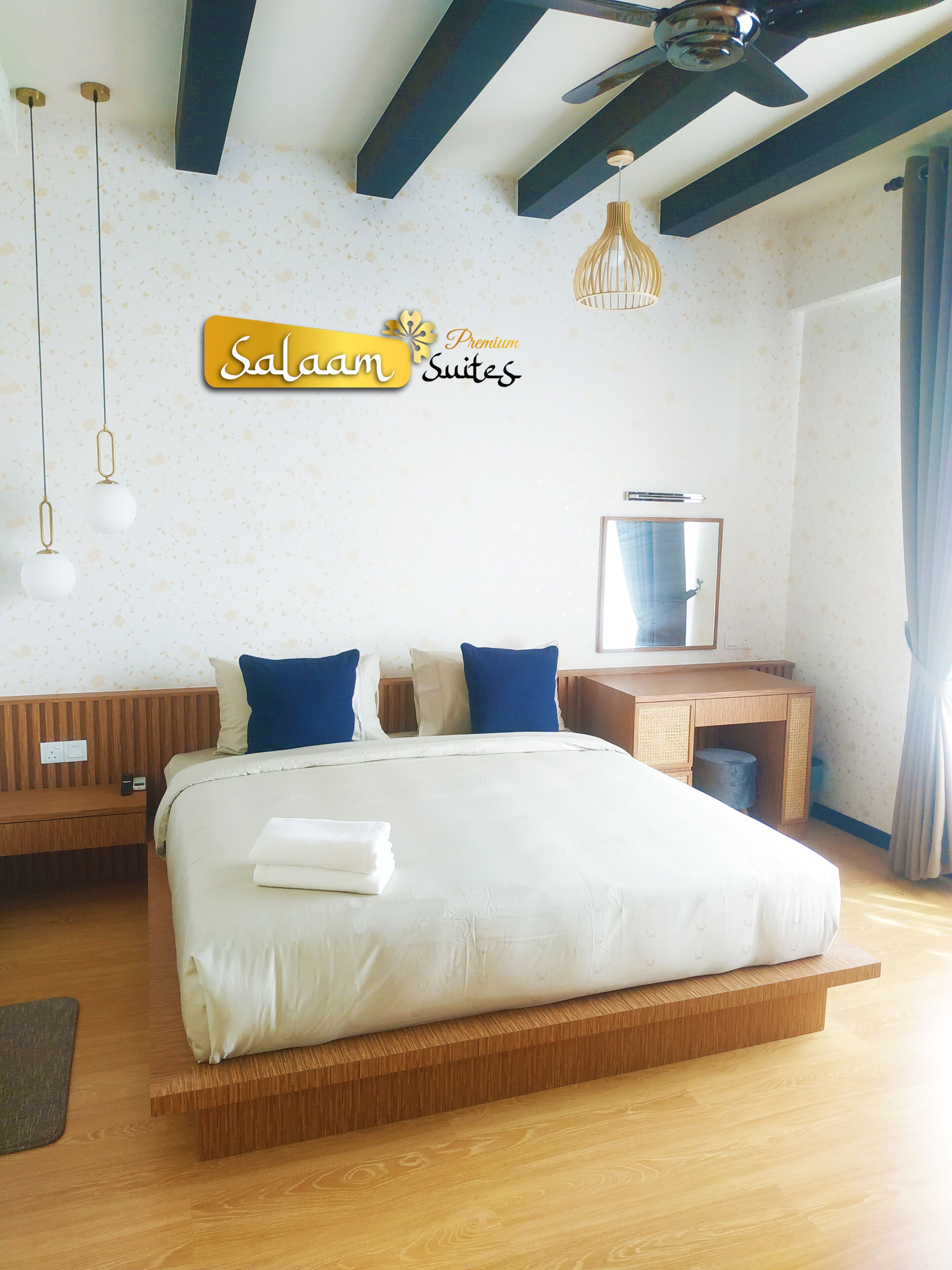 Quarto de hotel com uma cama grande, cabeceira de madeira, mesas de cabeceira, uma escrivaninha e um ventilador de teto.
