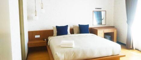 Quarto de hotel moderno com cama de madeira, mesa de cabeceira, espelho e secretária.