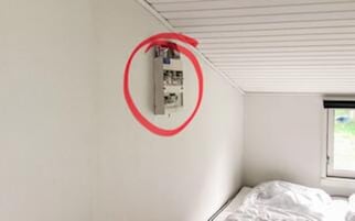 Quarto com teto branco, janela à direita e quadro elétrico na parede, circundado em vermelho.