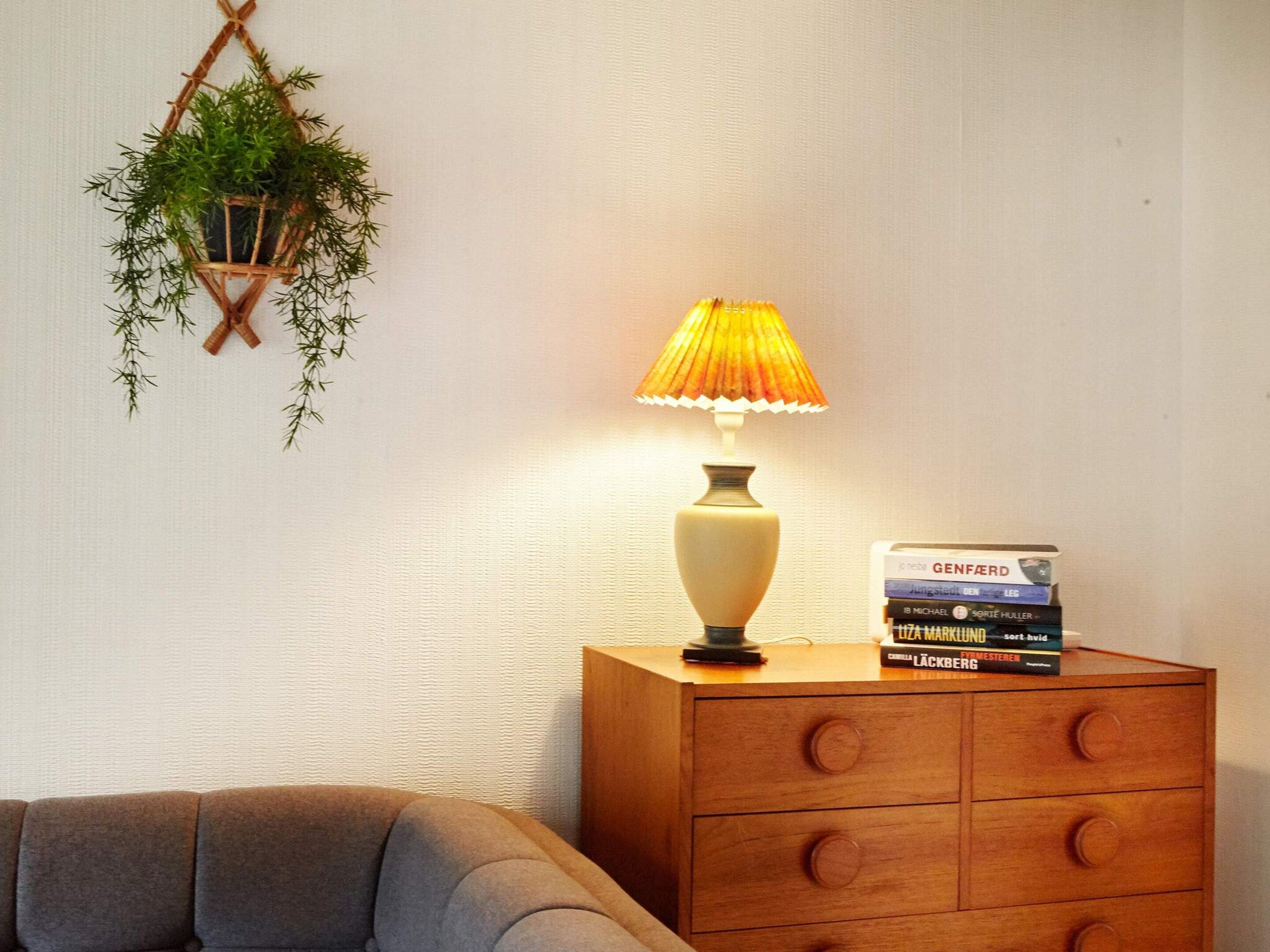 Uma mesa de cabeceira de madeira com uma luminária e uma pilha de livros.