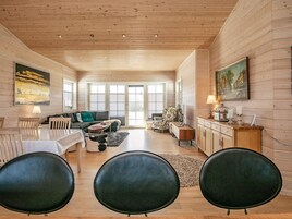 Uma sala de estar ampla com paredes de madeira, uma janela grande e um espaço de jantar com mesa e cadeiras.