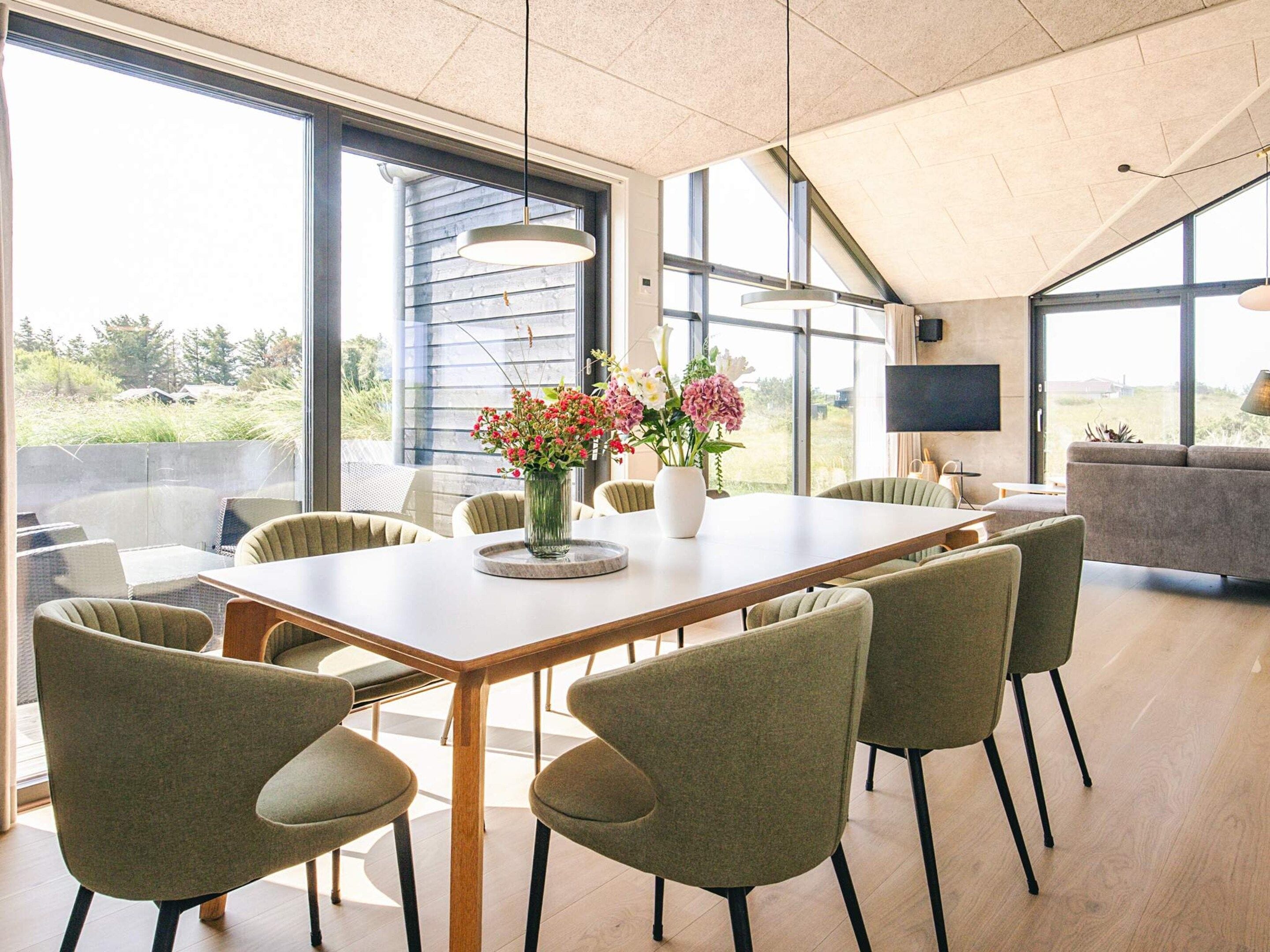Uma área de jantar moderna com uma mesa comprida, várias cadeiras e um vaso de flores.