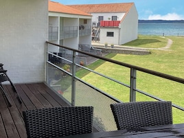 Varanda com mobiliário de vime com vista para uma área gramada e um edifício com telhado vermelho.