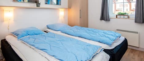 Quarto com duas camas, guarda-roupa, arte abstrata na parede, janela com cortinas e radiador.