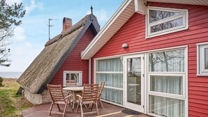 Uma casa vermelha com telhado de palha, um deck de madeira e uma mesa com cadeiras.