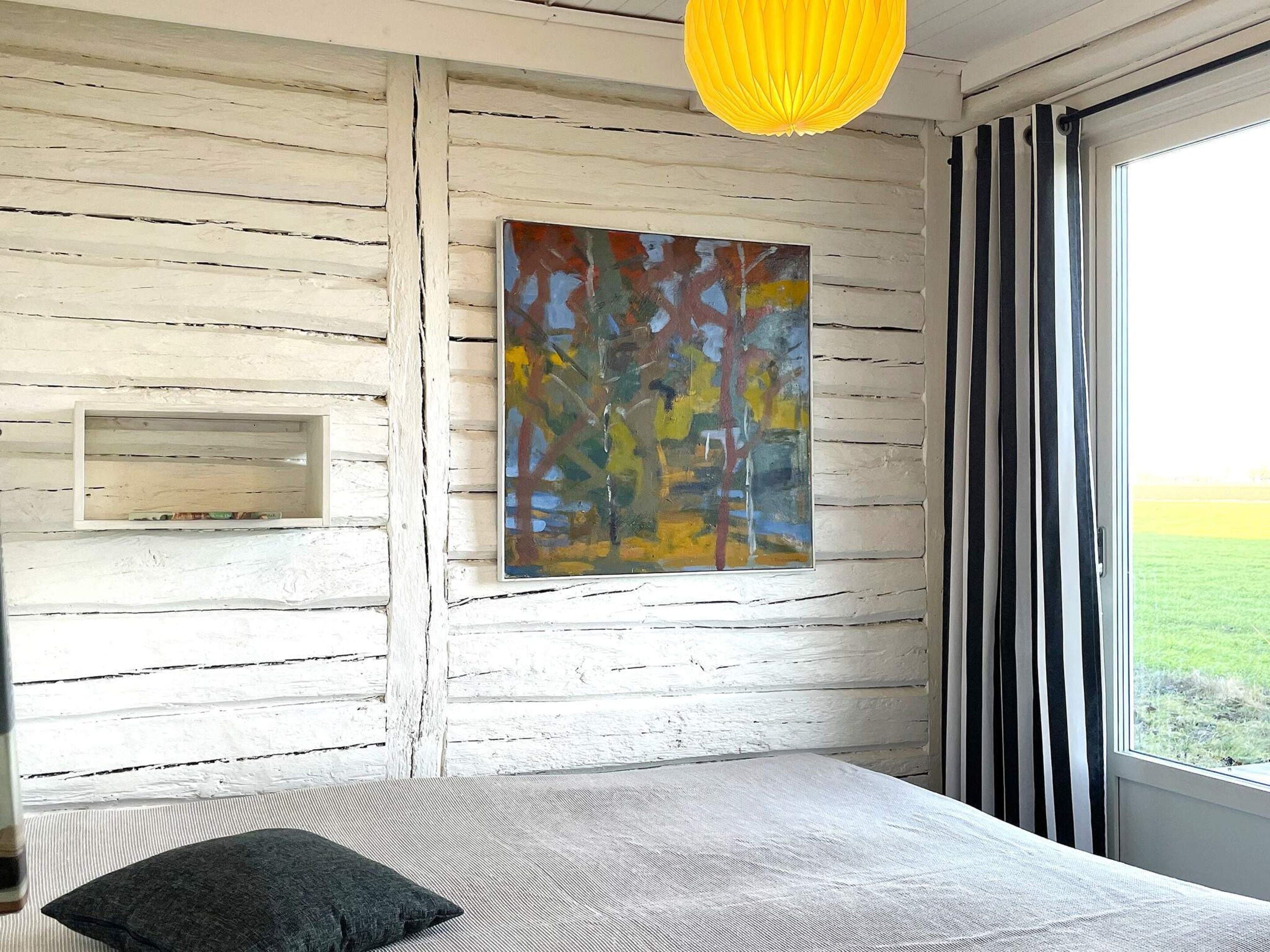 Quarto com cama, quadro, janela com cortinas e luminária pendente.