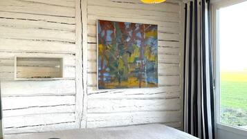 Quarto com cama, quadro, janela com cortinas e luminária pendente.