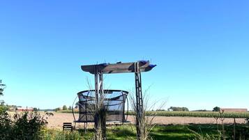 Um ambiente rural ao ar livre com uma estrutura de madeira, possivelmente um gazebo, e um cercado de tela metálica.