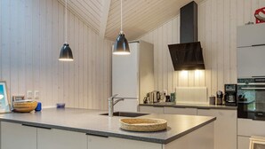 Uma cozinha moderna com ilha central, luminárias pendentes, fogão embutido e cafeteira.