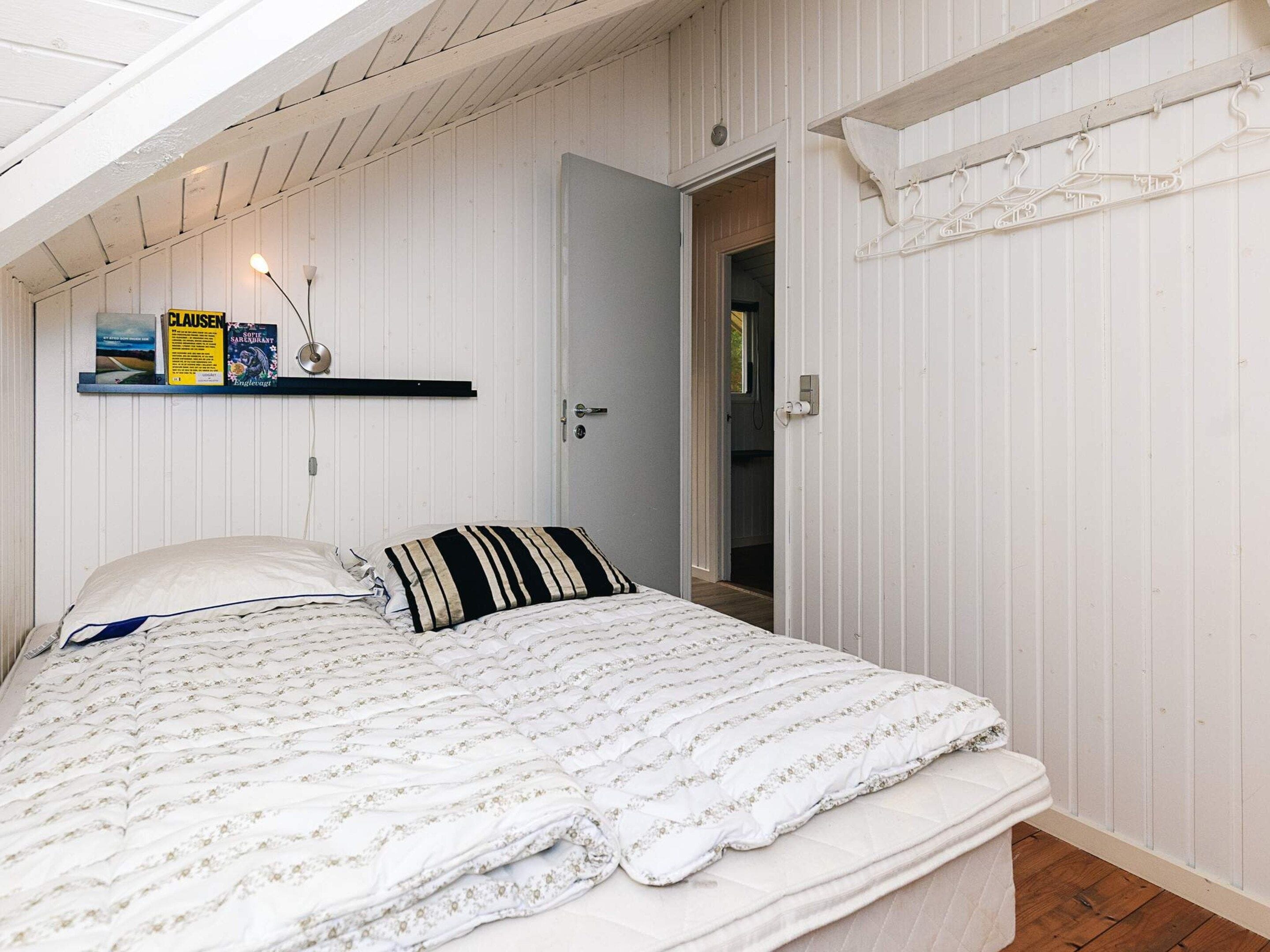 Quarto com uma cama, uma porta, uma estante com livros e uma janela.