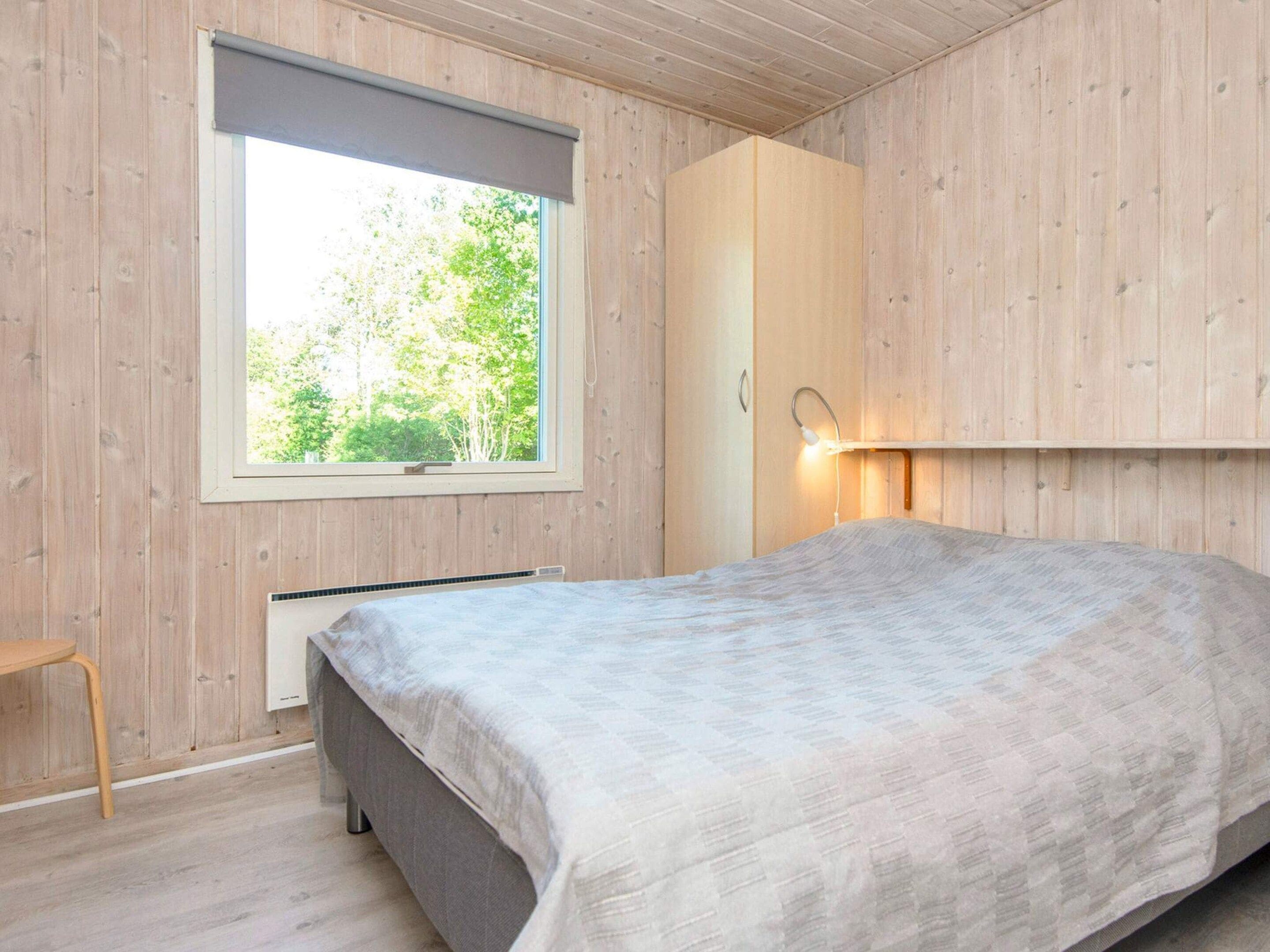 Quarto com cama, janela, radiador e parede de madeira.
