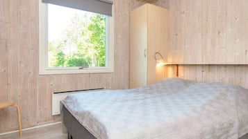 Quarto com cama, janela, radiador e parede de madeira.