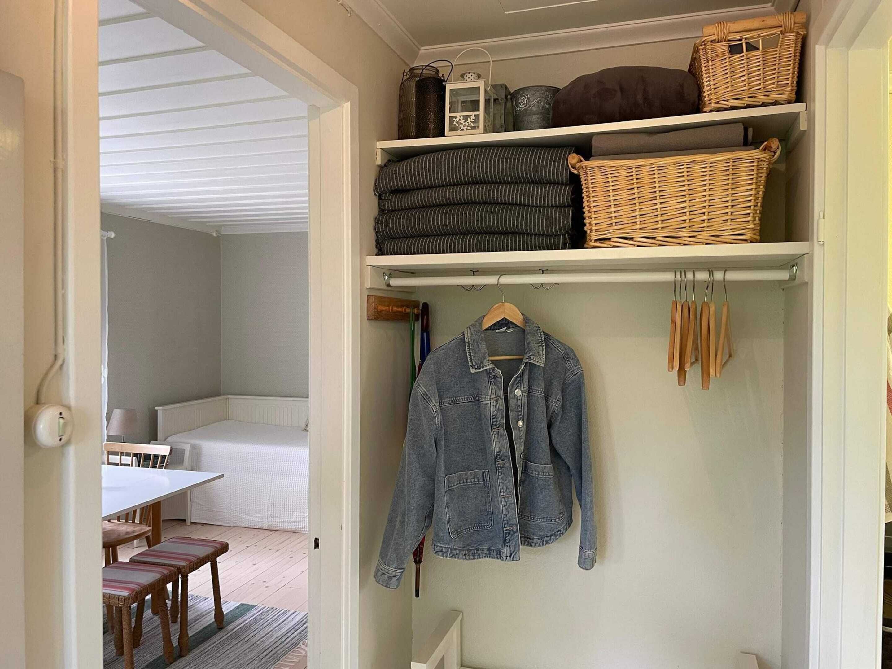 Um quarto com cama, mesa de jantar e armário com roupas dobradas e cestos.