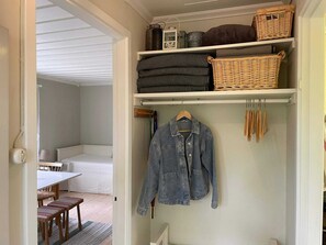 Um quarto com cama, mesa de jantar e armário com roupas dobradas e cestos.
