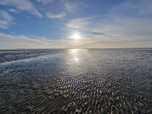 Uma praia com mar calmo, céu claro e o sol refletindo na água.
