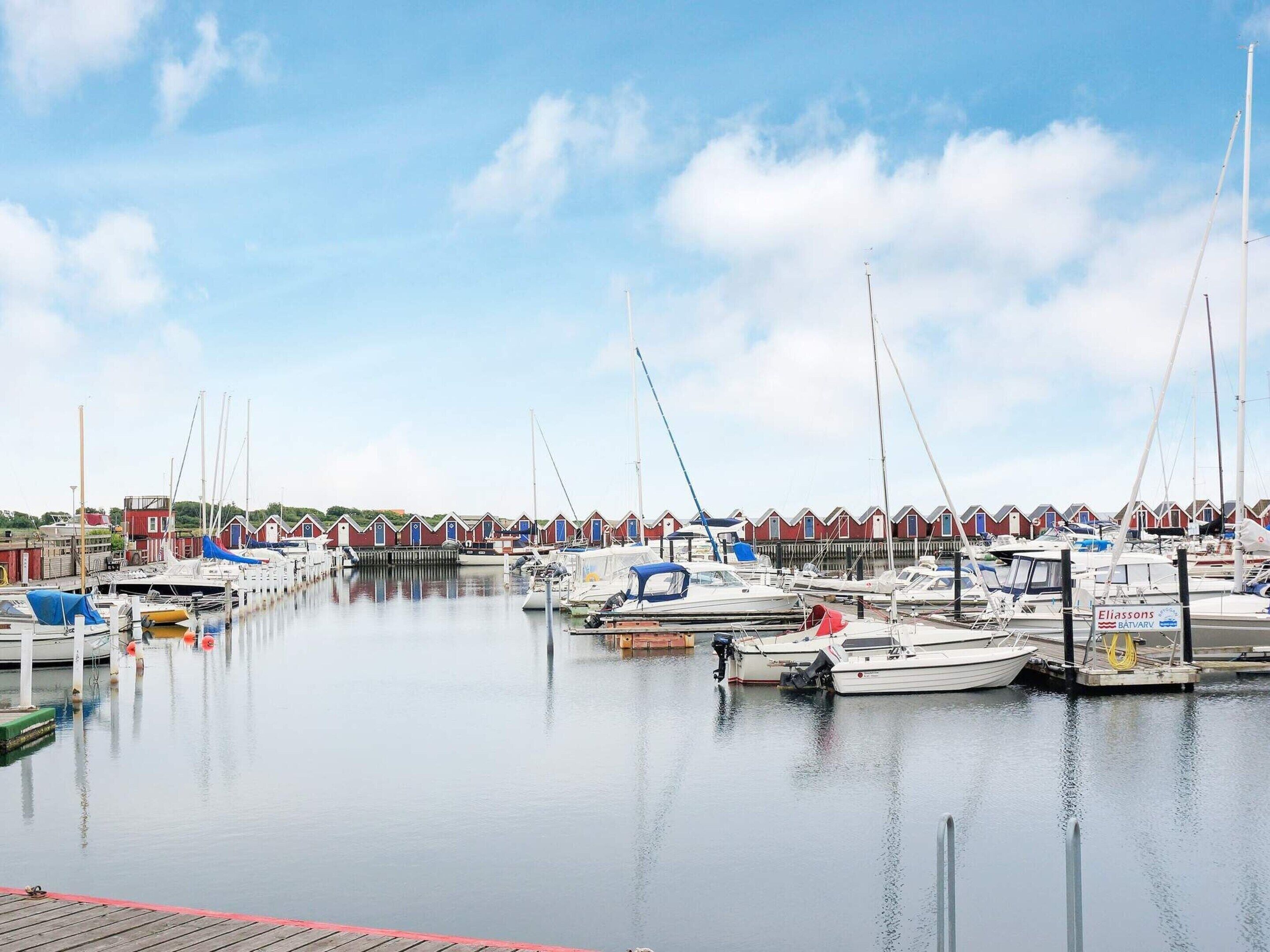 Marina com barcos atracados, fileira de edifícios vermelhos e azuis, e céu claro.