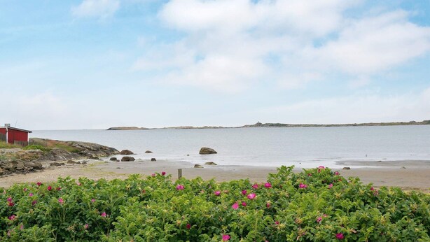 Paisagem costeira com uma praia de areia, um edifício vermelho e uma ilha ao longe.