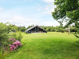 Uma casa moderna com um gramado extenso e uma área de refeições visível pelas janelas.