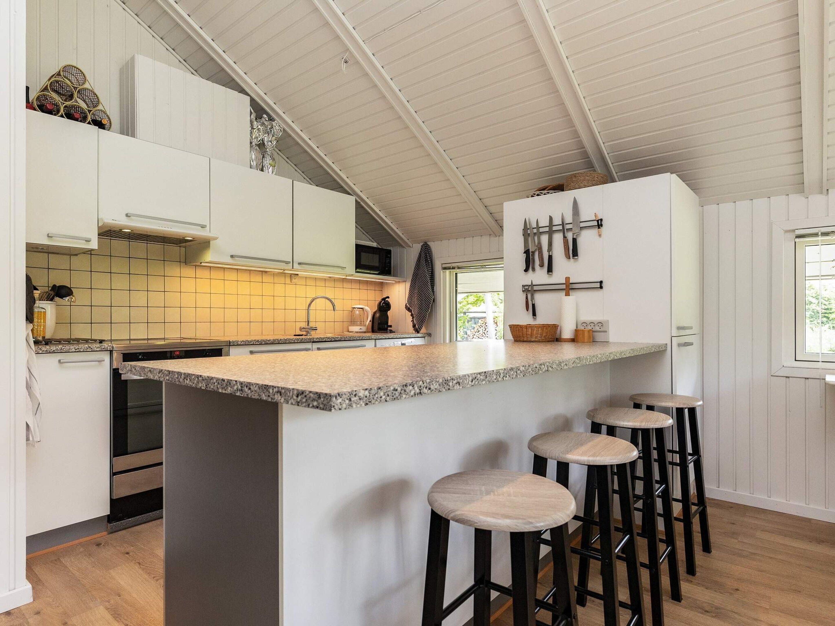 Cozinha com ilha central, banquetas, micro-ondas e suporte para facas.