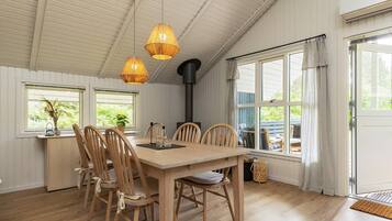 Uma área de refeições com mesa e cadeiras de madeira, luminárias pendentes, janela com cortinas e vista para o exterior.