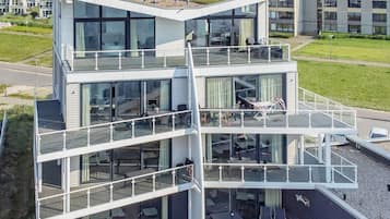 Um edifício moderno, com vários andares, varandas de vidro e áreas de estar ao ar livre.