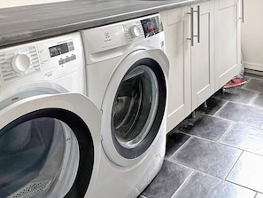 Máquina de lavar roupa de abertura frontal com visor digital e painel de comandos, localizada em uma cozinha moderna com armários brancos e piso ladrilhado.