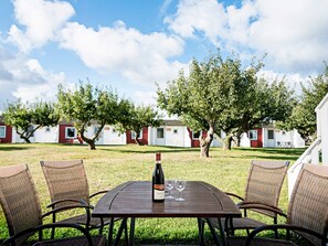 Uma mesa de madeira com duas cadeiras em área externa gramada, uma garrafa de vinho e dois copos.
